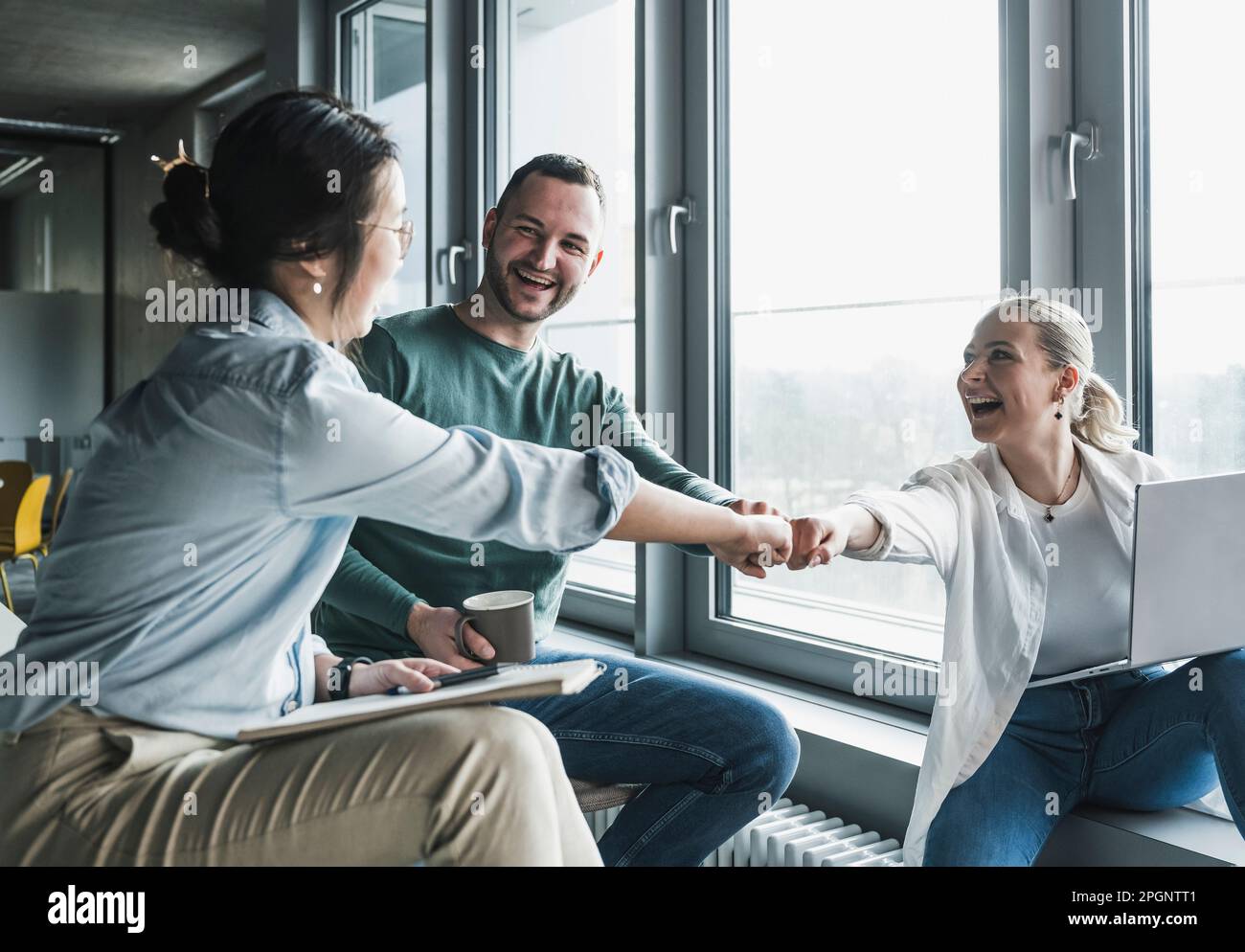 Cheerful business colleagues giving fist bumps to each other at office ...