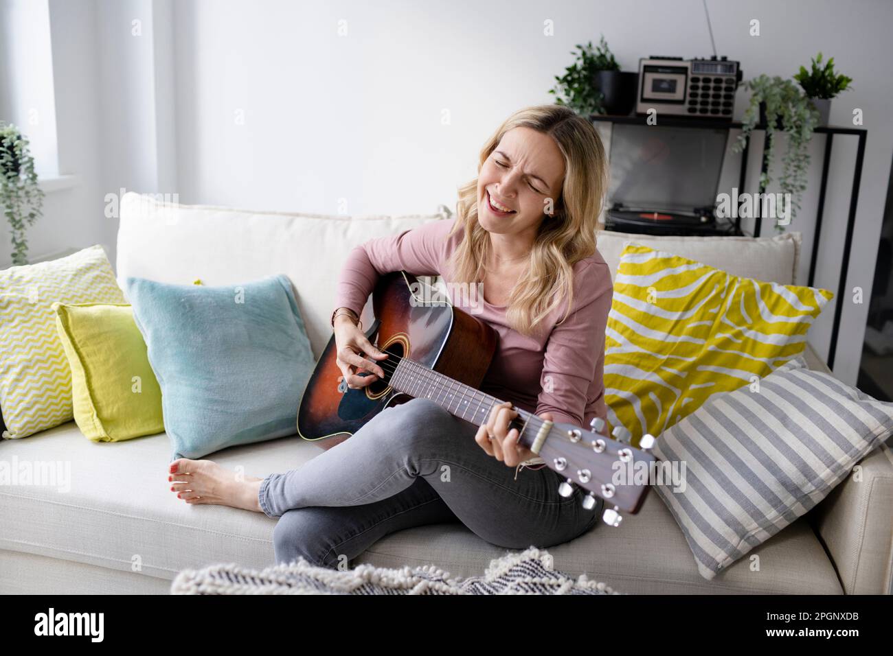 Happy mature woman singing and playing guitar on sofa at home Stock ...