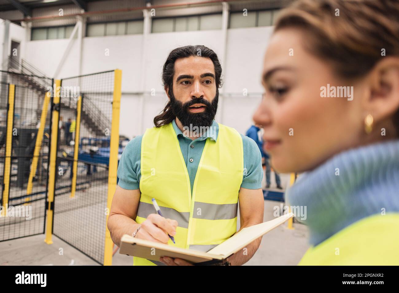 Engineer with note pad explaining colleague in factory Stock Photo - Alamy