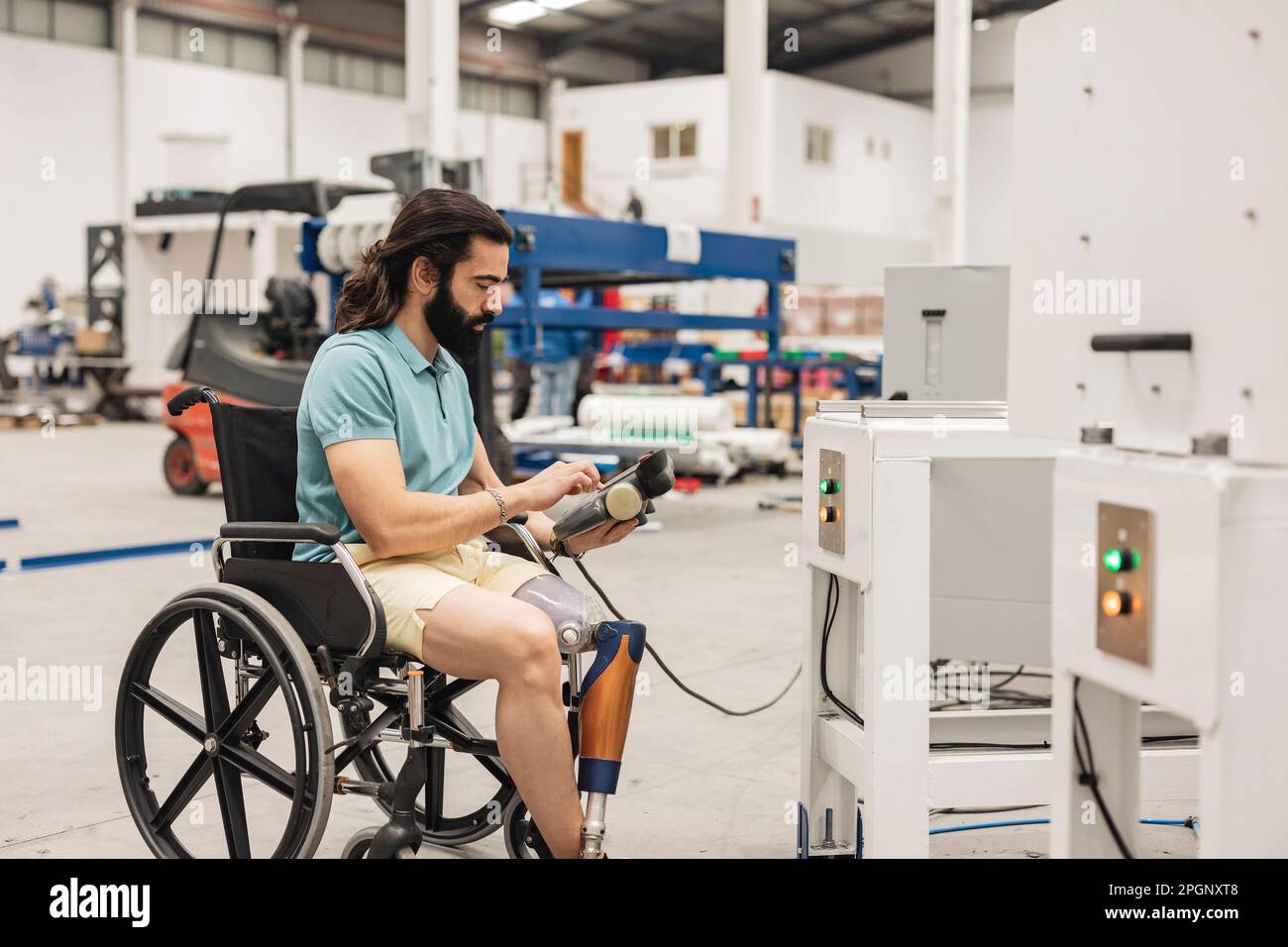 Engineer sitting in wheelchair using controller of machine in industry ...