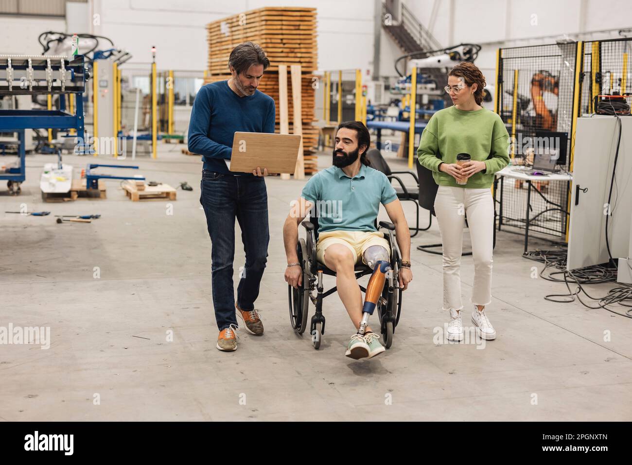 Engineer sitting in wheelchair with colleagues in robotics factory ...