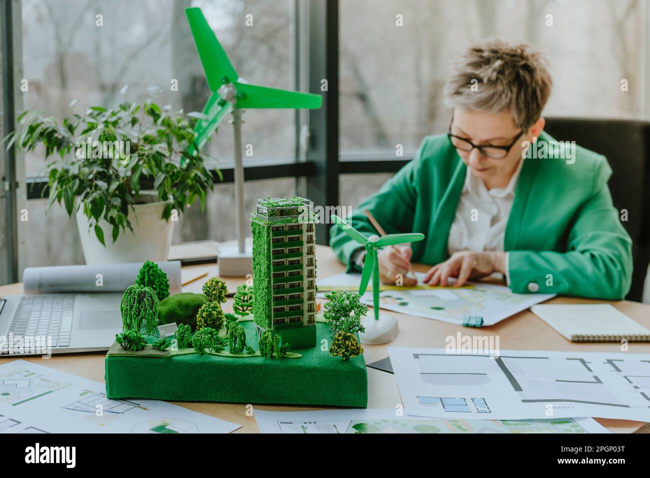 Architect working on blueprint by building and wind turbine models at ...