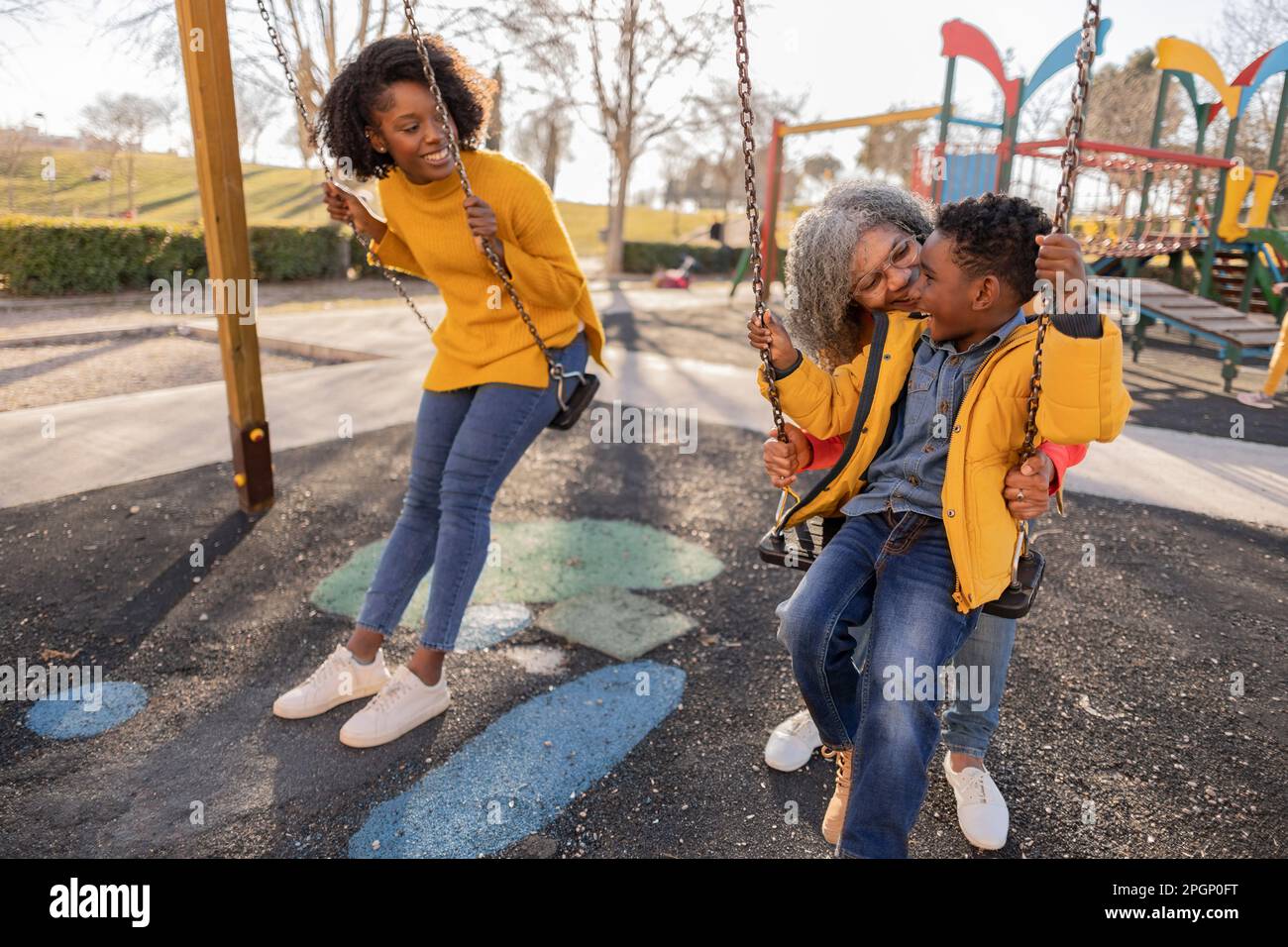 Happy woman looking at mother pushing grandson on swing on playground ...