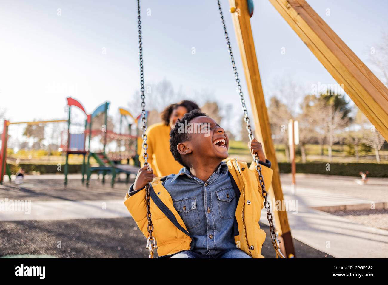 Mother pushing son on swing at playground Stock Photo - Alamy