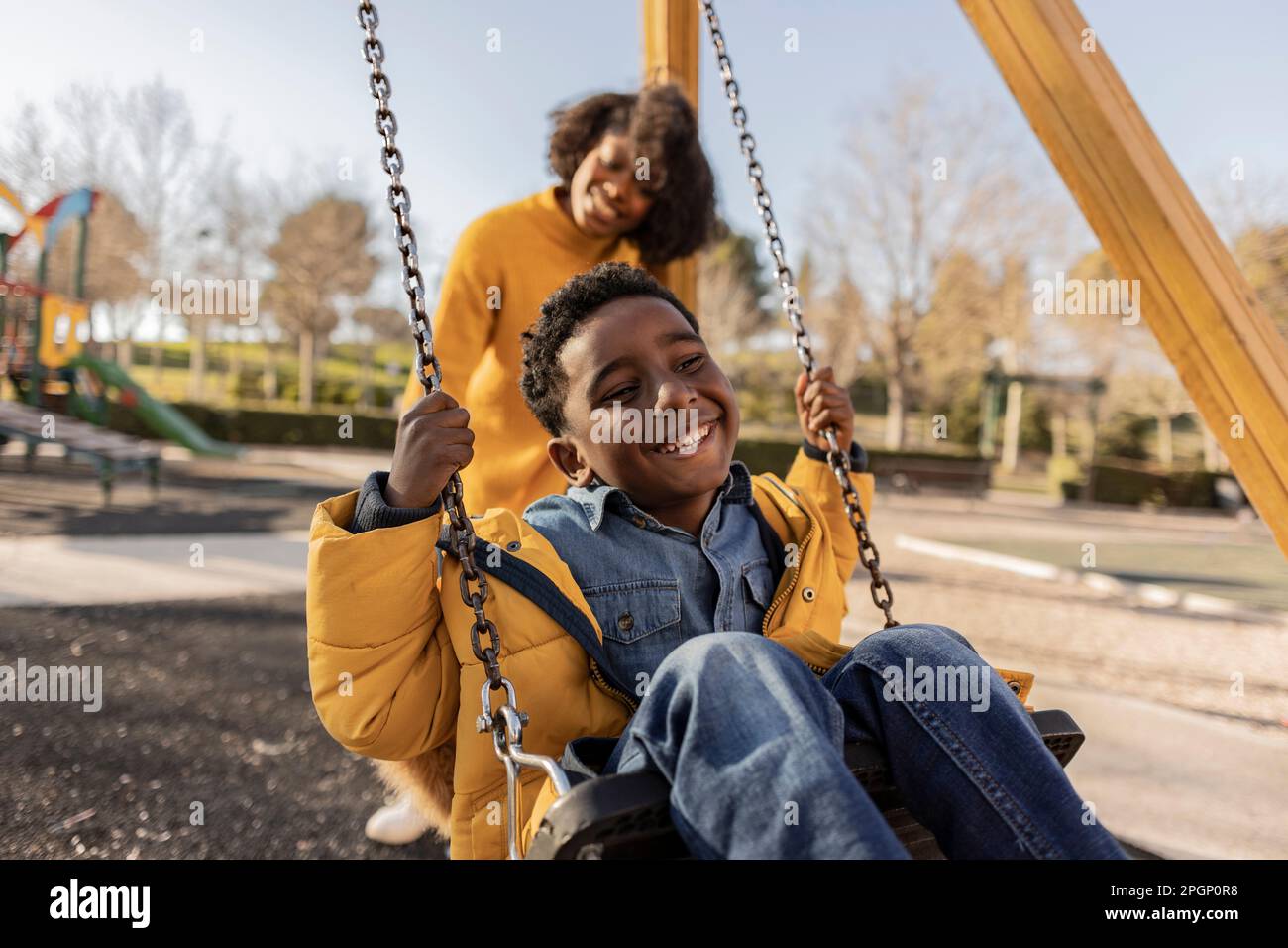 Happy mother pushing son on swing at playground Stock Photo - Alamy
