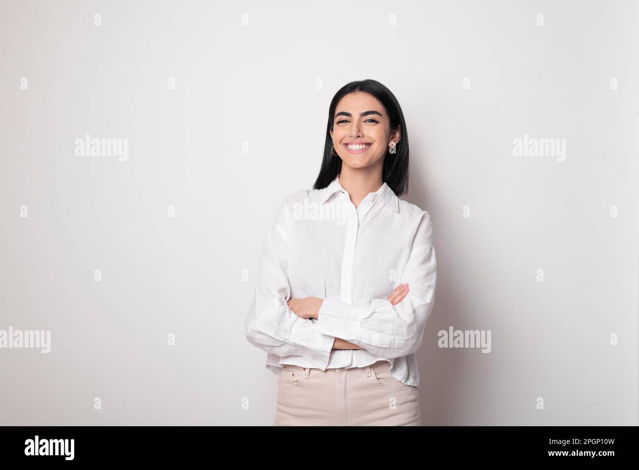 Smiling woman with arms crossed standing against white background Stock ...