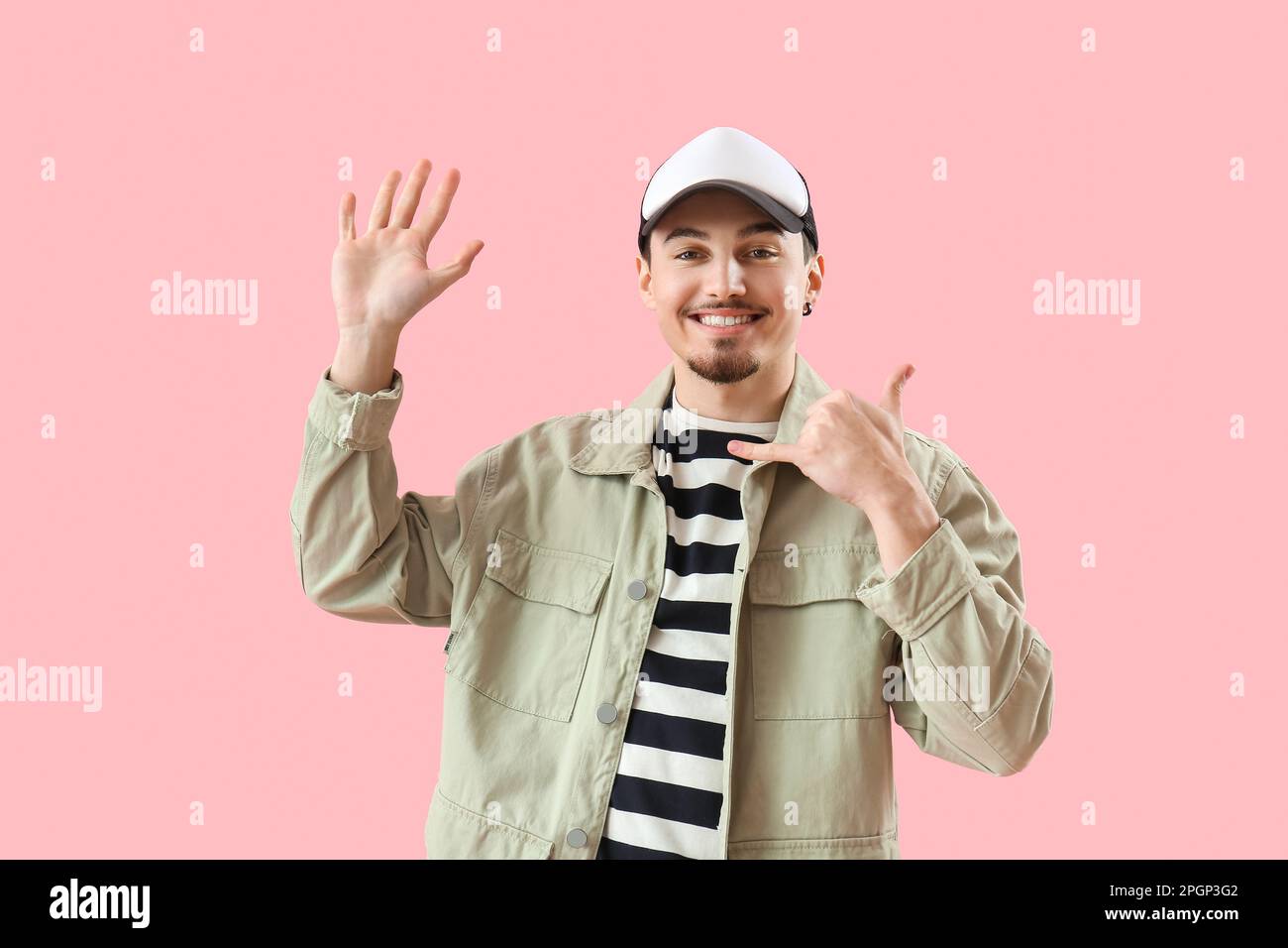 Cool young man showing "call me" gesture and waving hand on pink ...