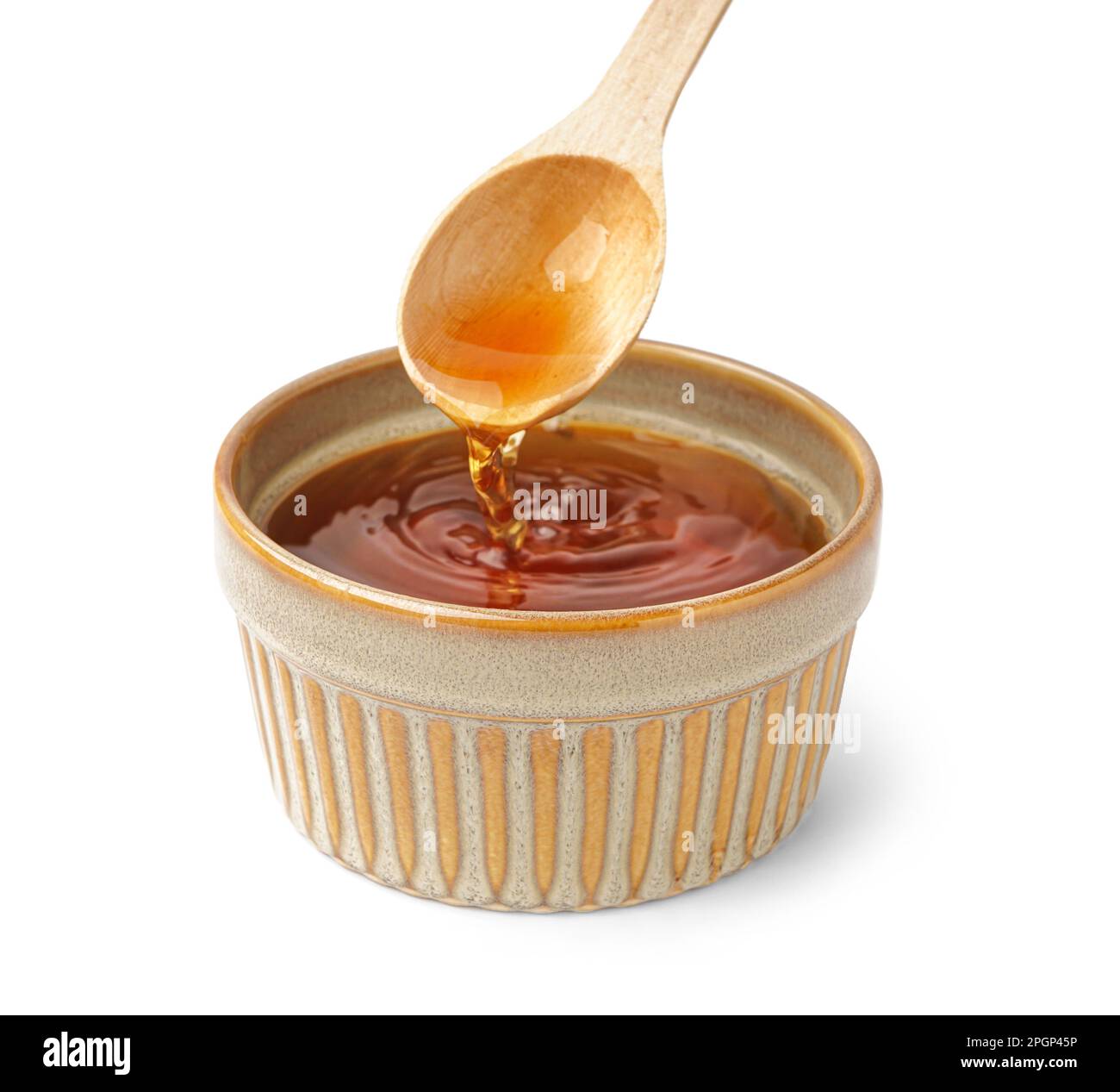 Pouring of tasty maple syrup from spoon into bowl on white background ...