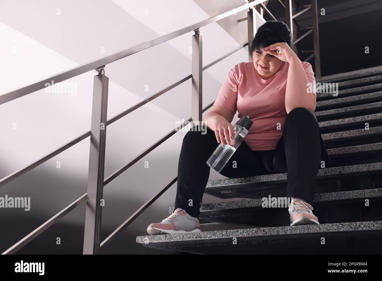 Tired overweight mature woman with bottle of water sitting on stairs ...
