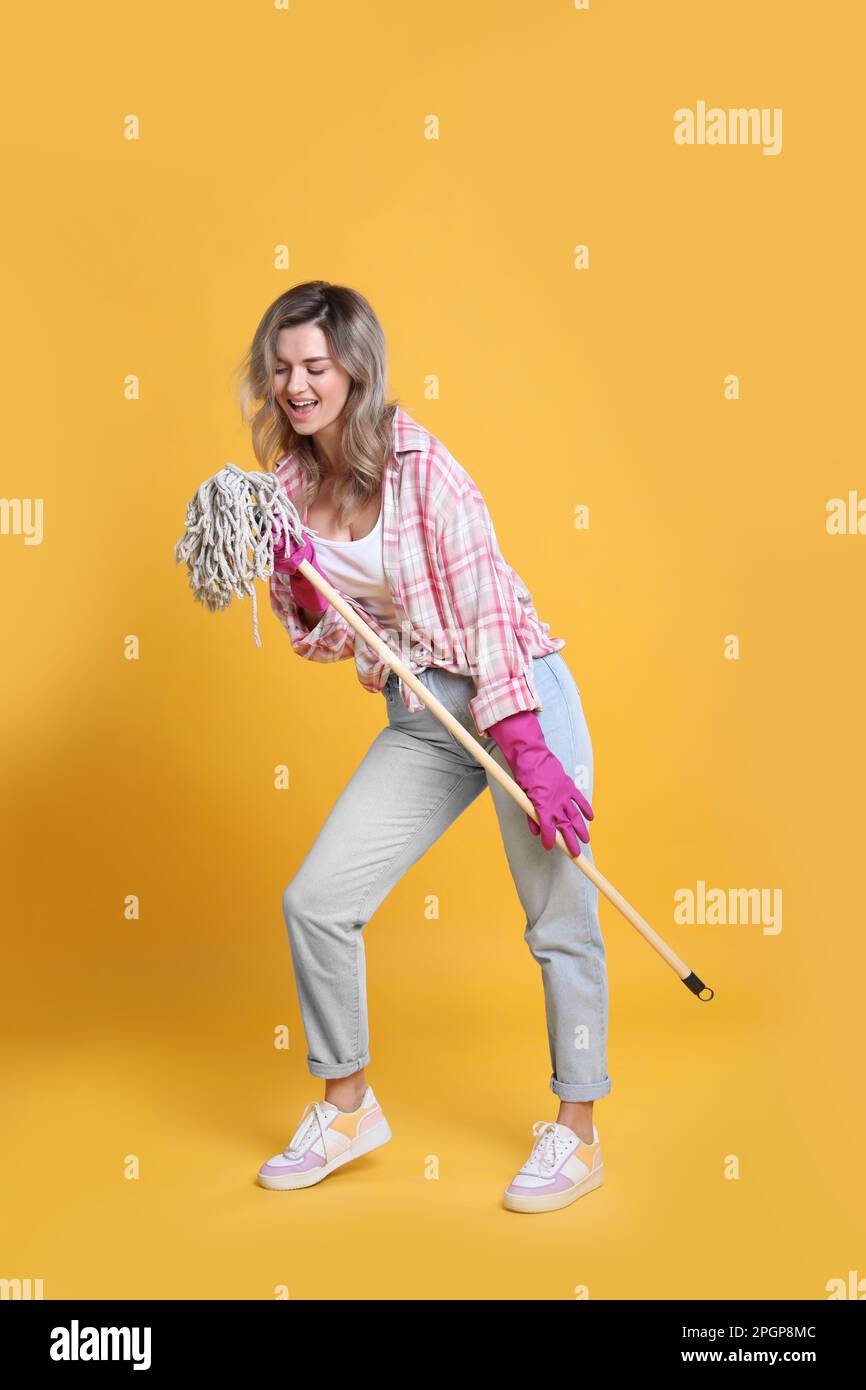 Beautiful young woman with mop singing on orange background Stock Photo ...