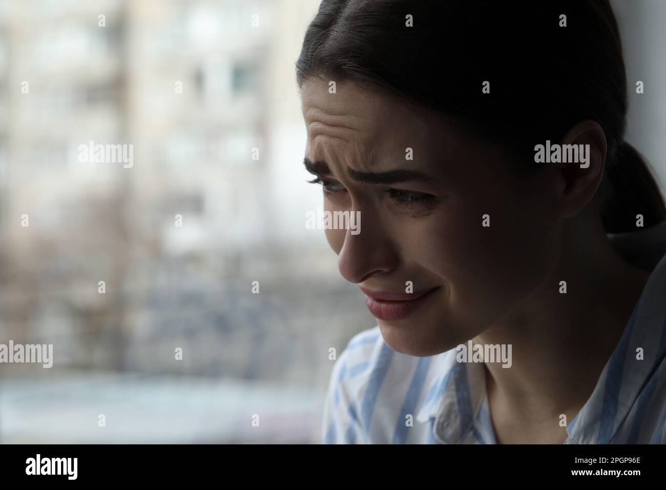 Sad young woman crying near window indoors, closeup with space for text ...