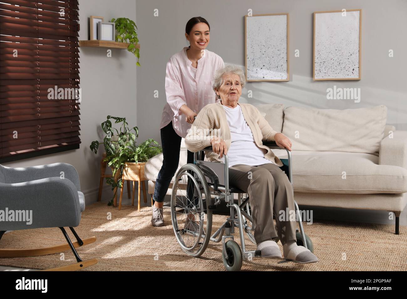Young Caregiver Assisting Senior Woman In Wheelchair Indoors Home Care