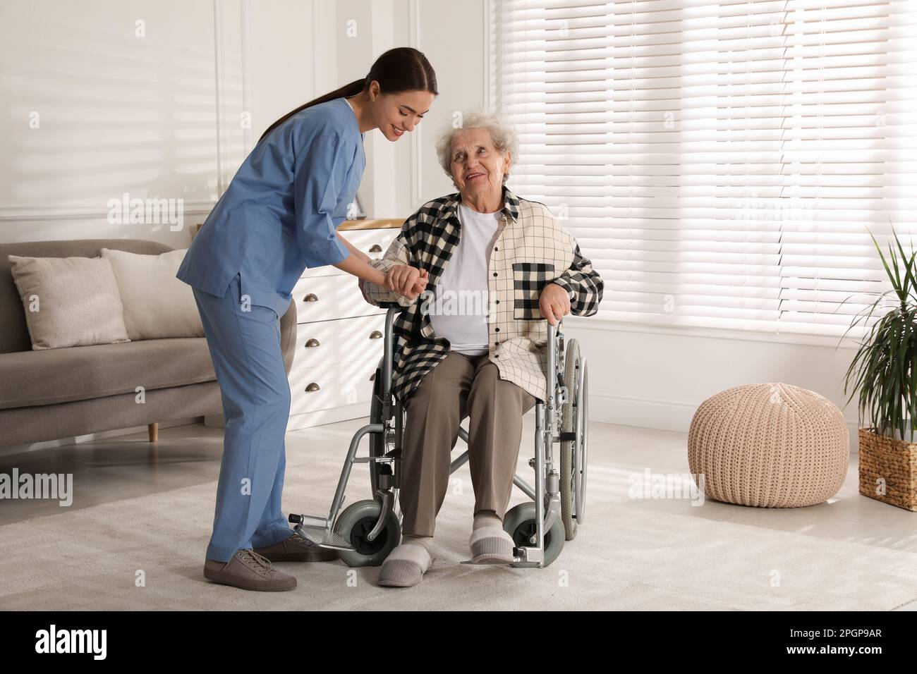 Young caregiver assisting senior woman in wheelchair indoors. Home ...