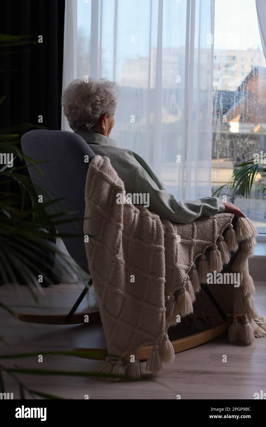 Elderly woman sitting in rocking chair indoors, back view. Loneliness ...