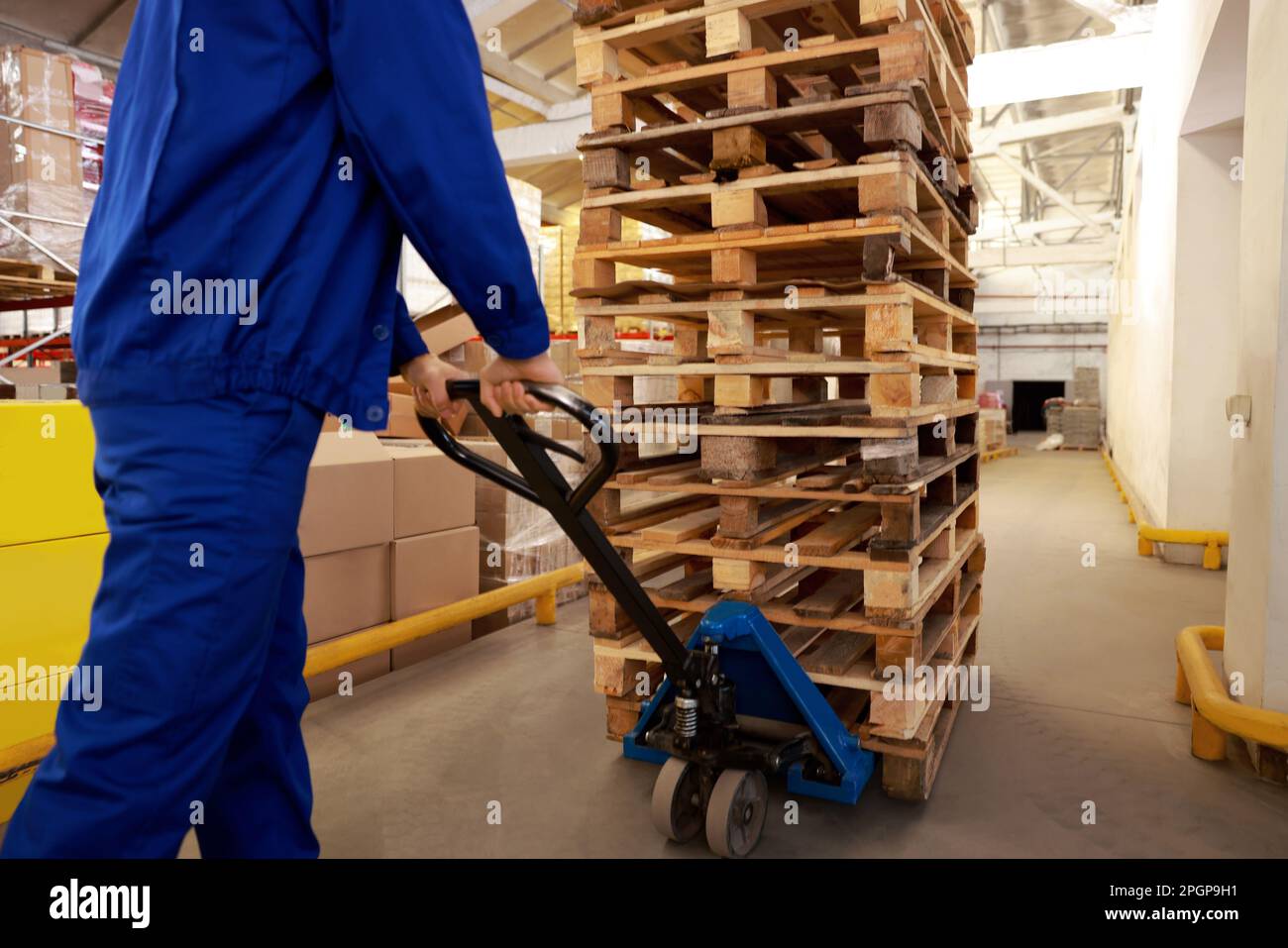 Worker moving wooden pallets with manual forklift in warehouse, closeup ...