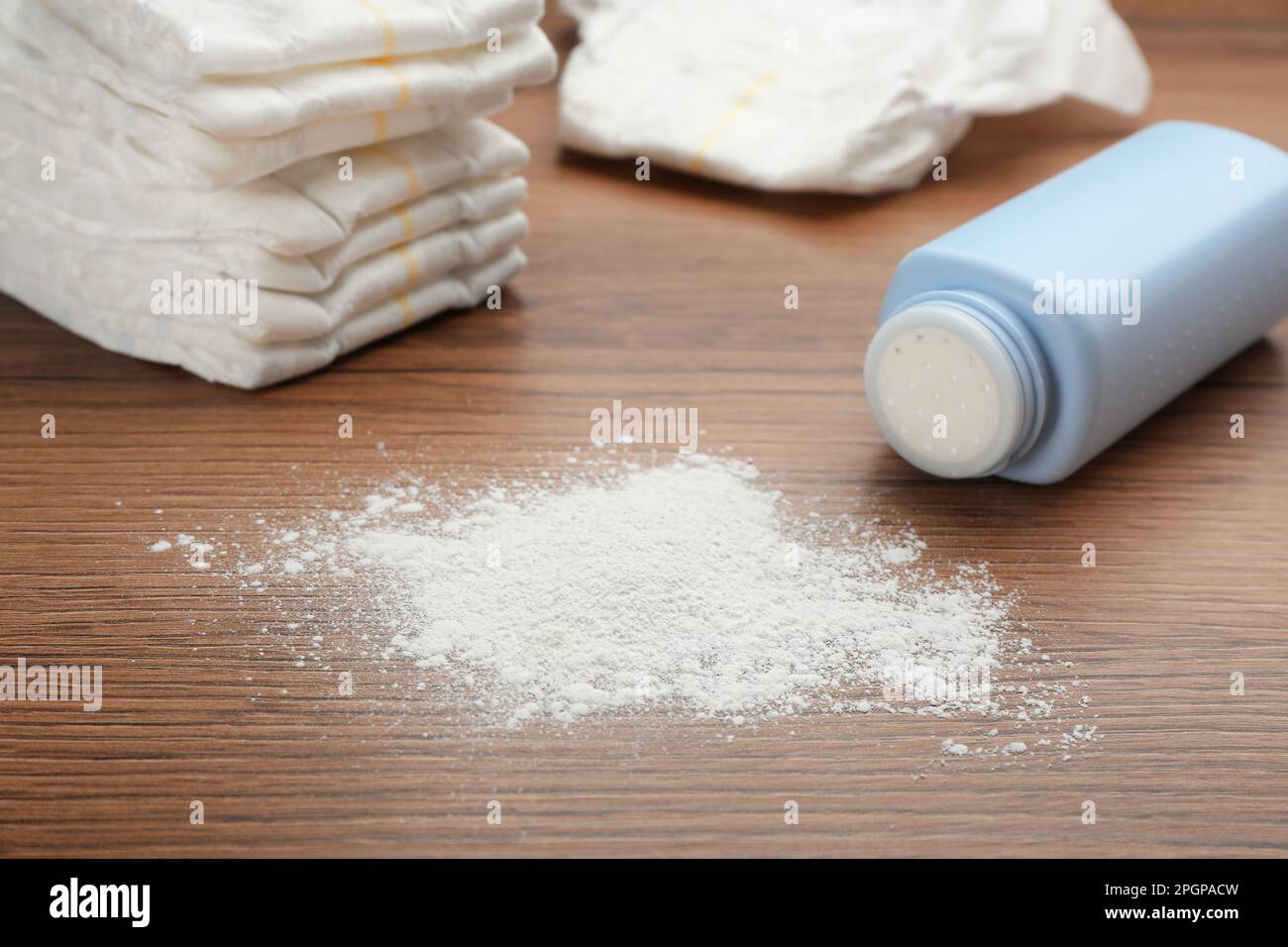 Bottle, scattered dusting powder and diapers on wooden background. Baby ...