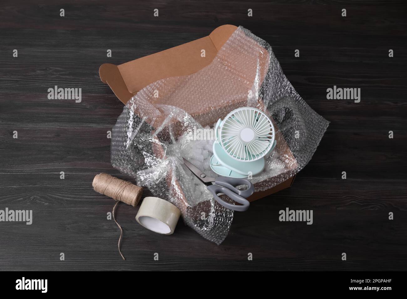 Small fan with bubble wrap in cardboard box and packaging items on dark ...