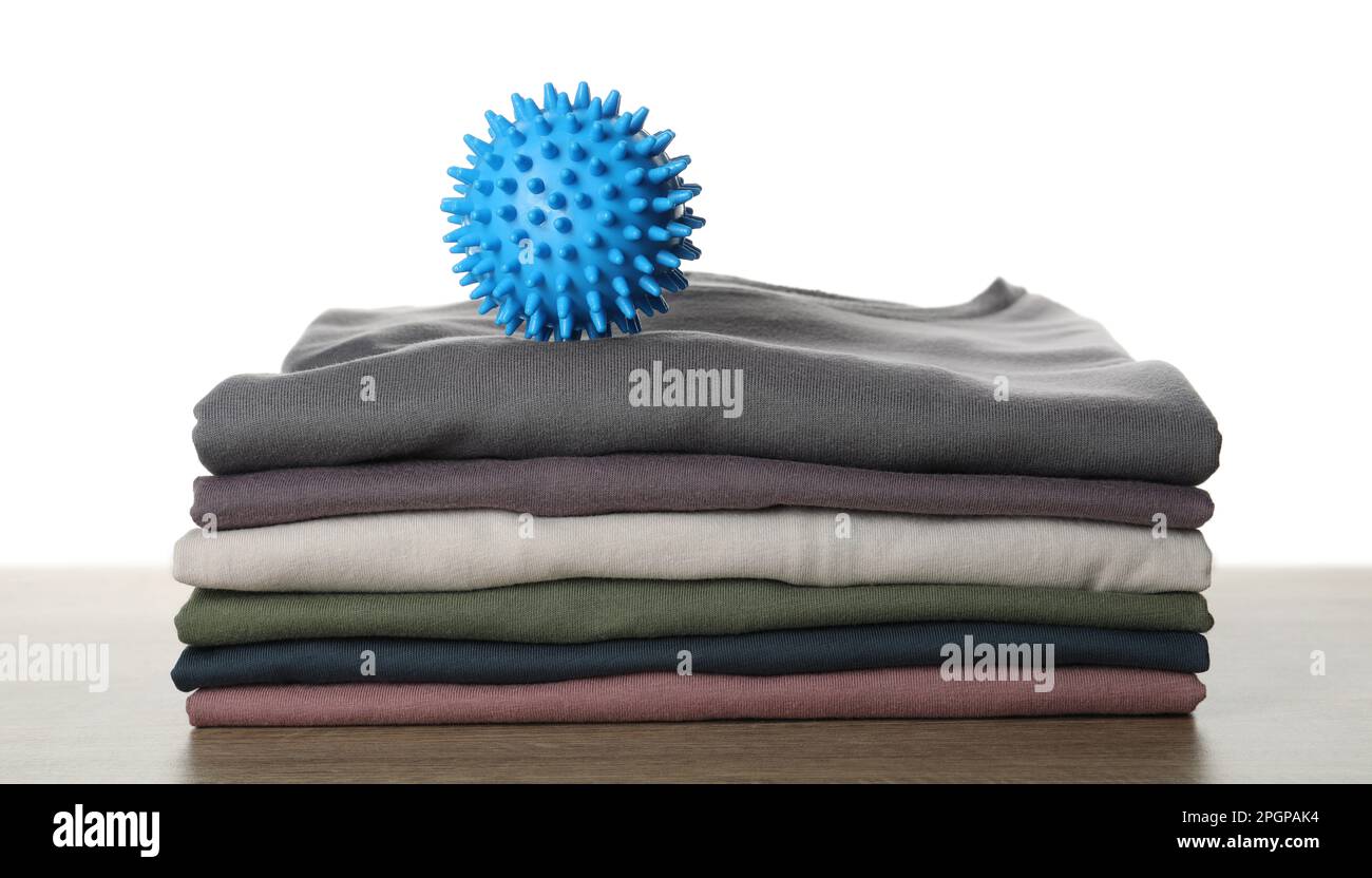 Blue dryer ball and stacked clean clothes on wooden table against white ...