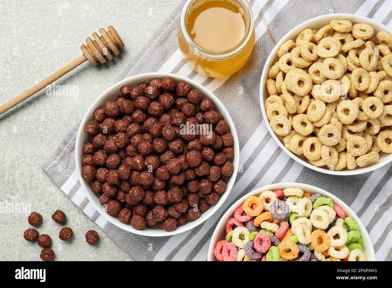 Different delicious breakfast cereals and honey on light grey table ...