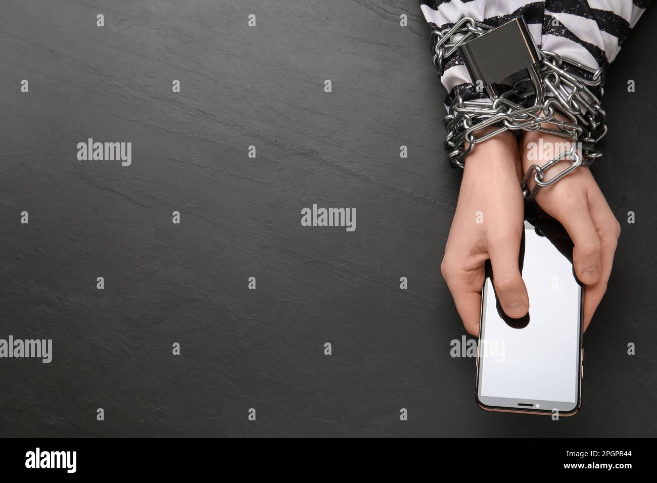 Prisoner holding smartphone in chained hands at black table, top view ...