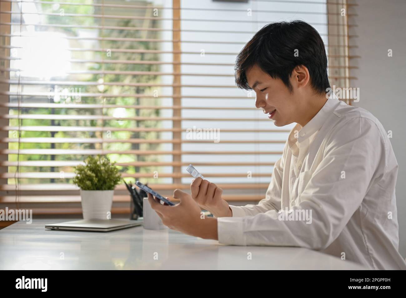 Side view of a handsome millennial Asian man using mobile banking ...