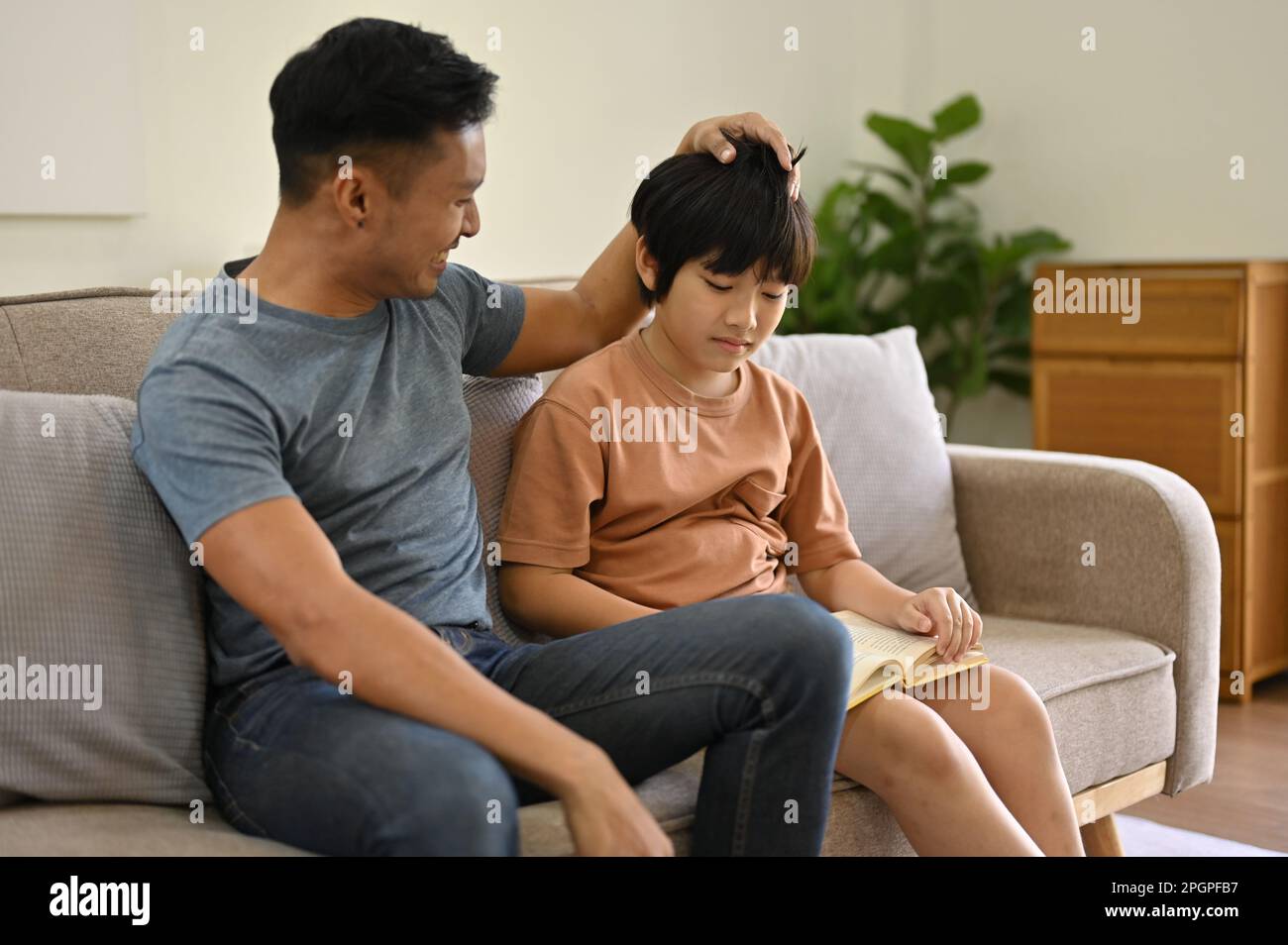 Kind and happy Asian dad is teaching his son to read or reading a ...