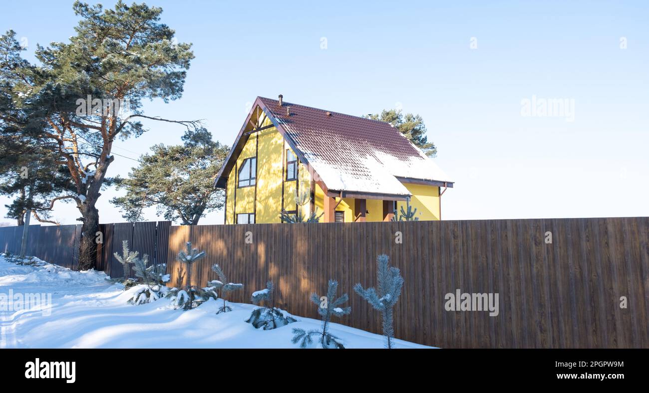 A yellow cozy house in the snow in winter in the village is surrounded ...