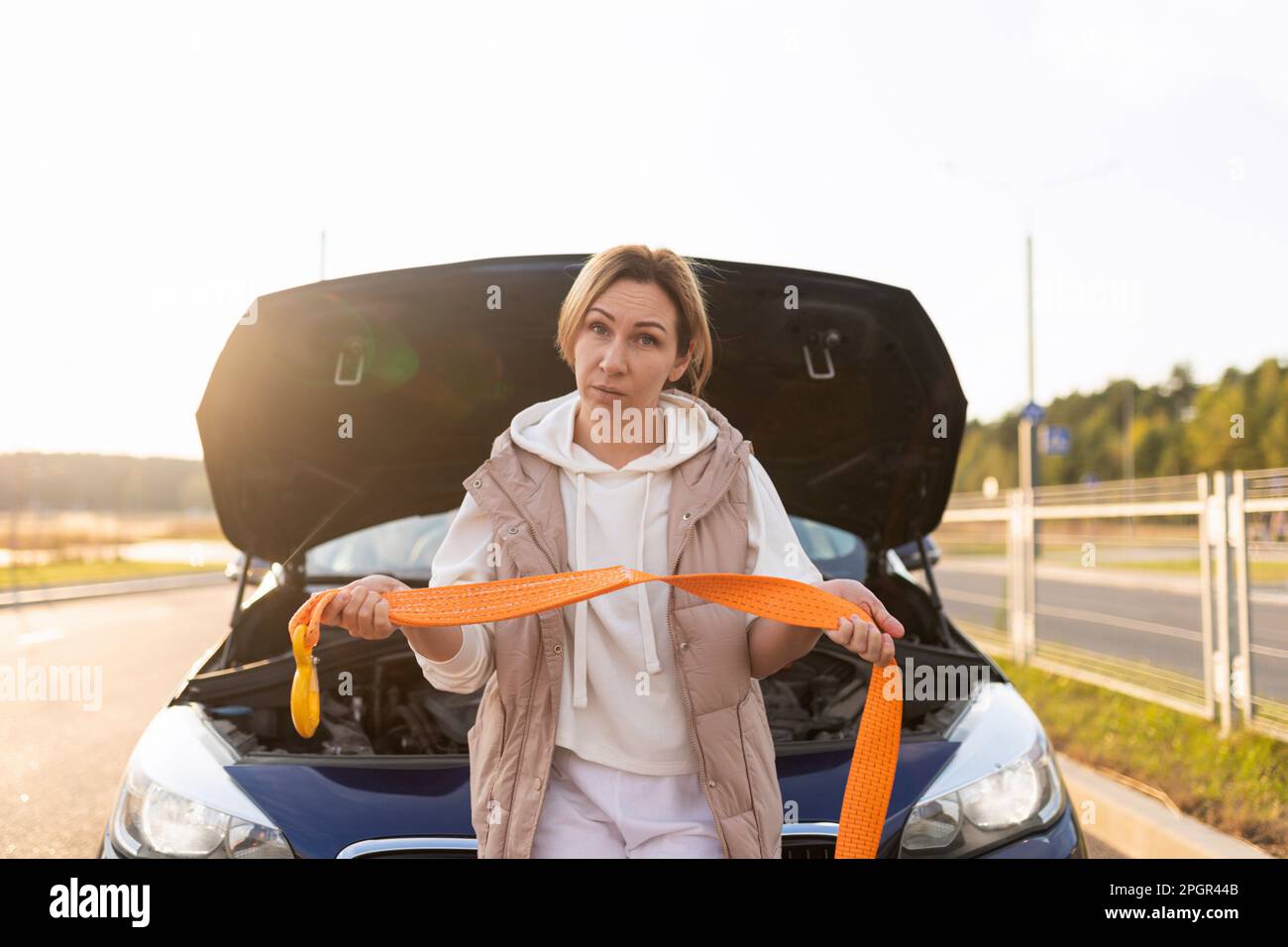 sad woman driver with a cable for towing a car in her hands against the ...
