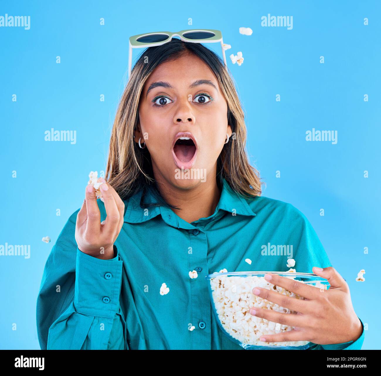 3D glasses, popcorn and wow with a woman in studio on a blue background looking shocked while ...