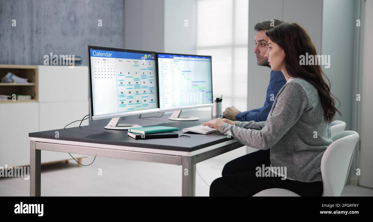 Young Businesspeople Analyzing Gantt Chart And Calendar On Computer In ...