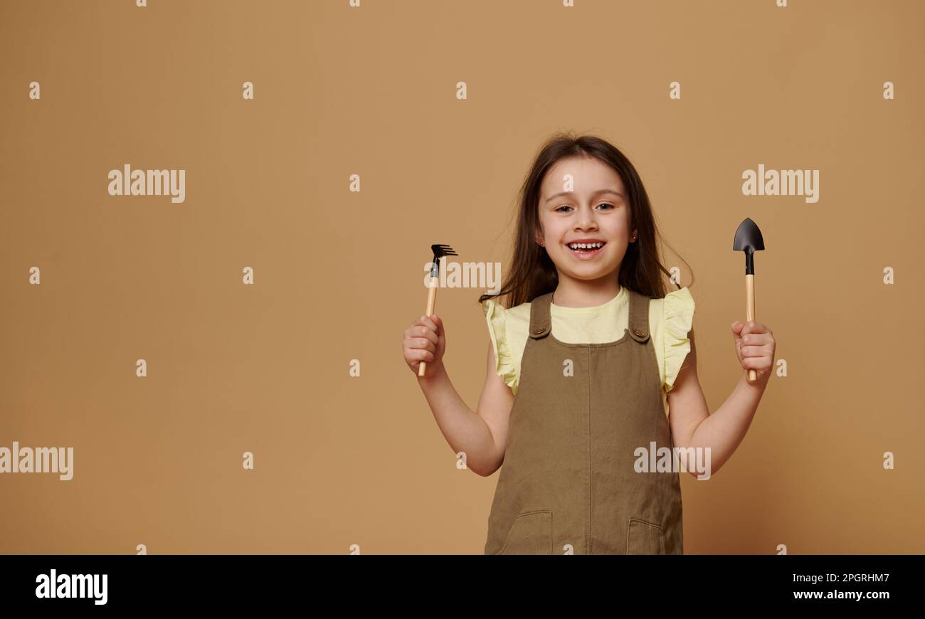 Happy child girl dressed in yellow t-shirt and khaki overalls, holding ...