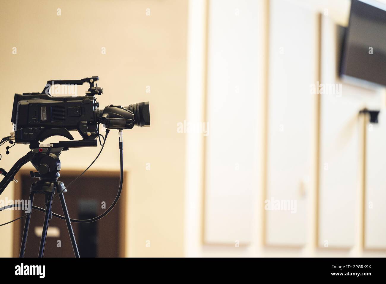 A professional video camera is set up on a tripod in a well-lit room ...
