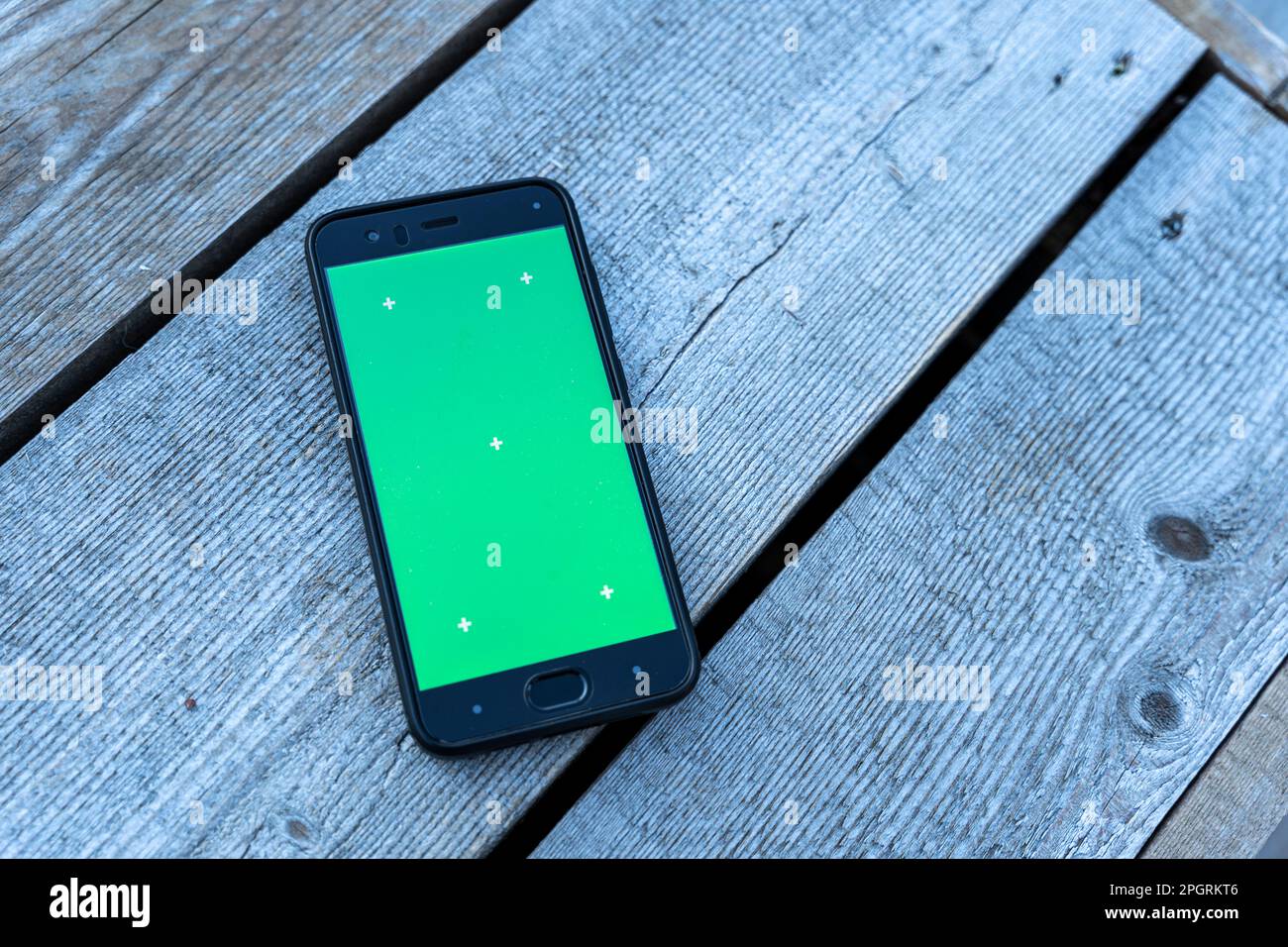a smartphone with a green screen lies on a faded wooden background ...