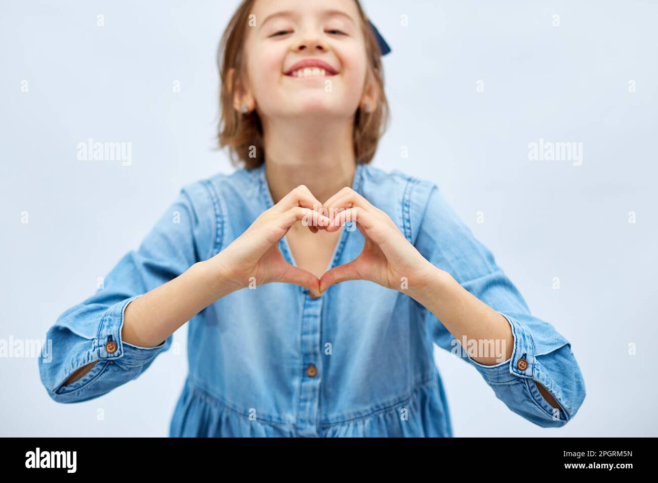Smiling little girl make heart sign with hands in casual denim dress ...