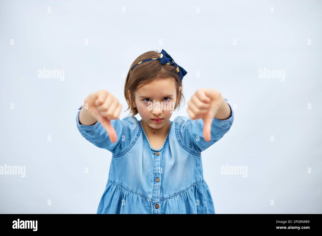 Unhappy teen girl child wearing jeans dress make thumb down in studio ...