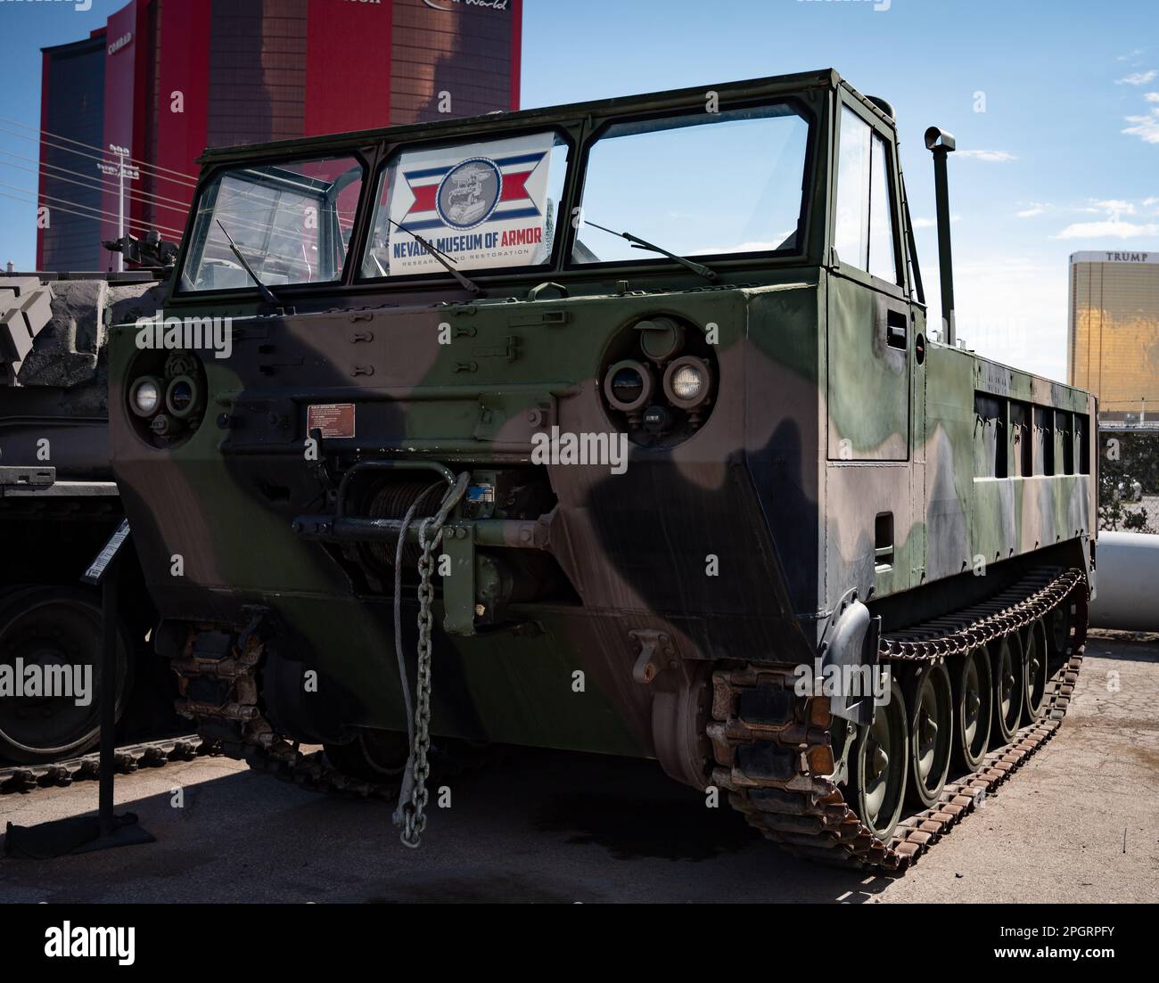 An olive-green military vehicle is parked in front of a red building ...