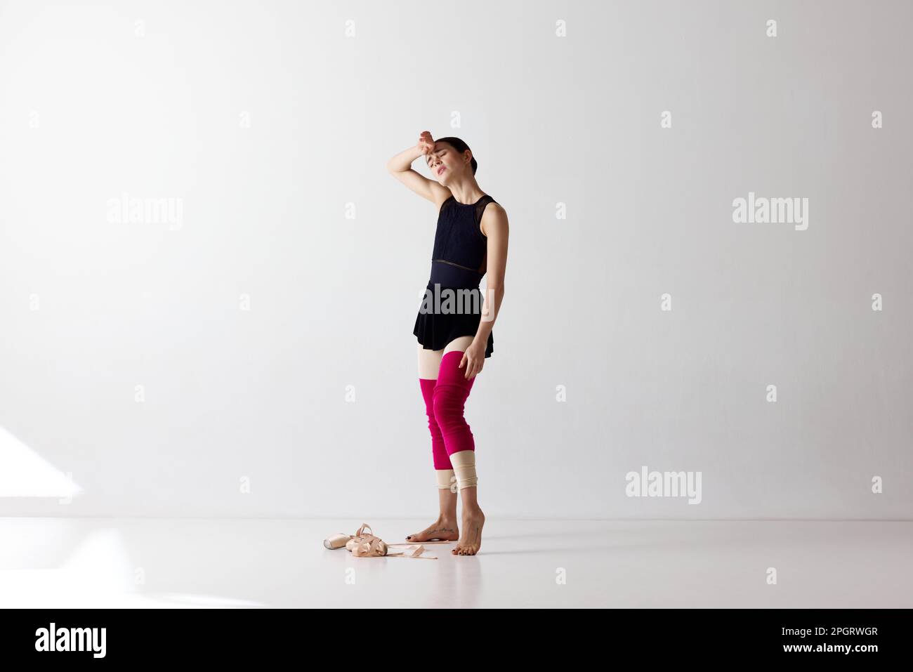 Exhausted beautiful ballerina standing and holding hand at head to rest ...
