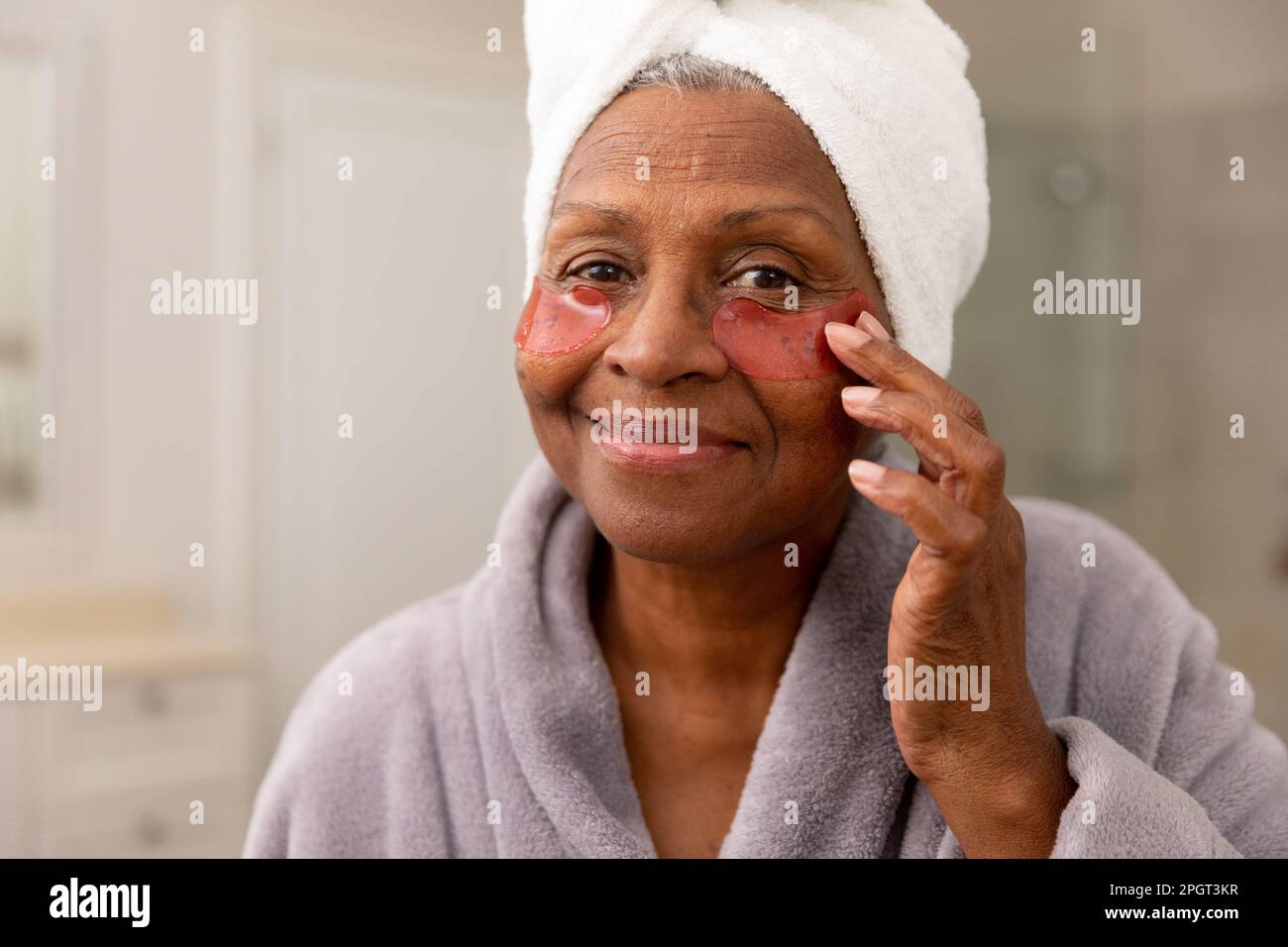 African american senior woman dressed in bathrobe applying eye patches ...