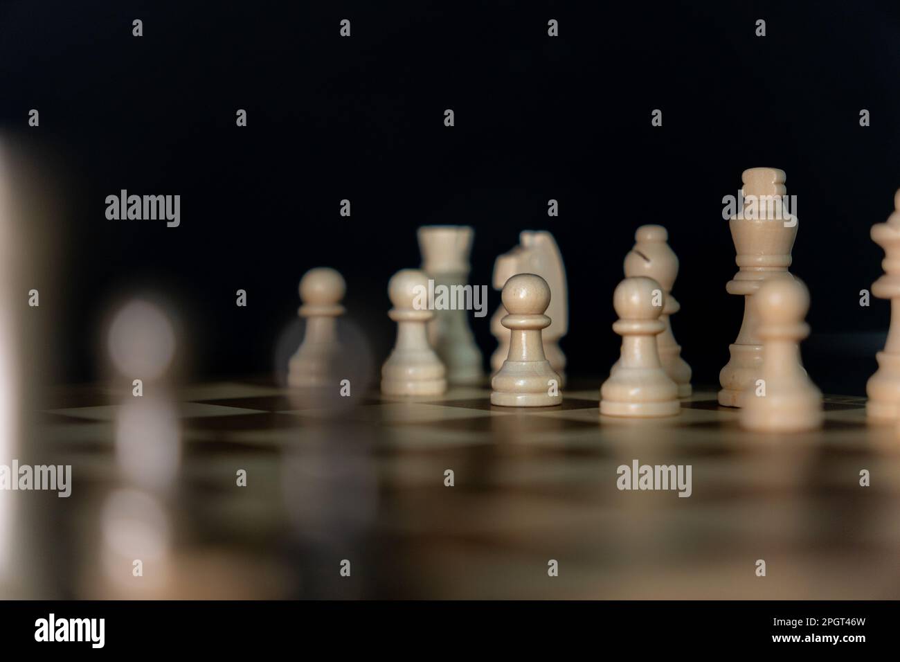 A white chess board is illuminated in a dark room, with the chess ...