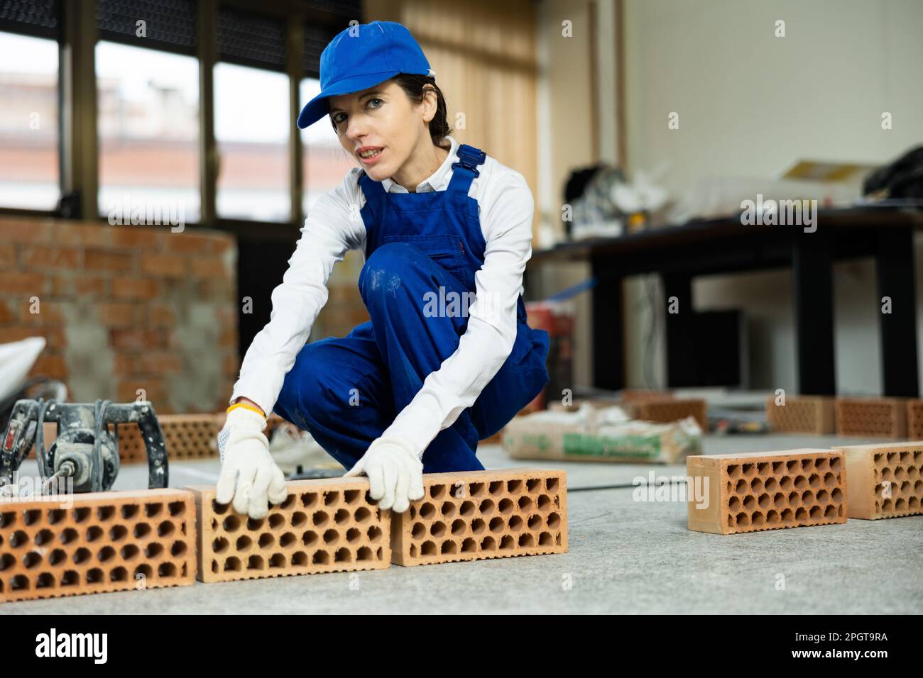 Female builder arranging bricks inside building under construction ...