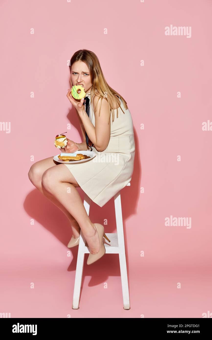 Shot of young adorable woman sitting and eating sweet donut with hungry ...