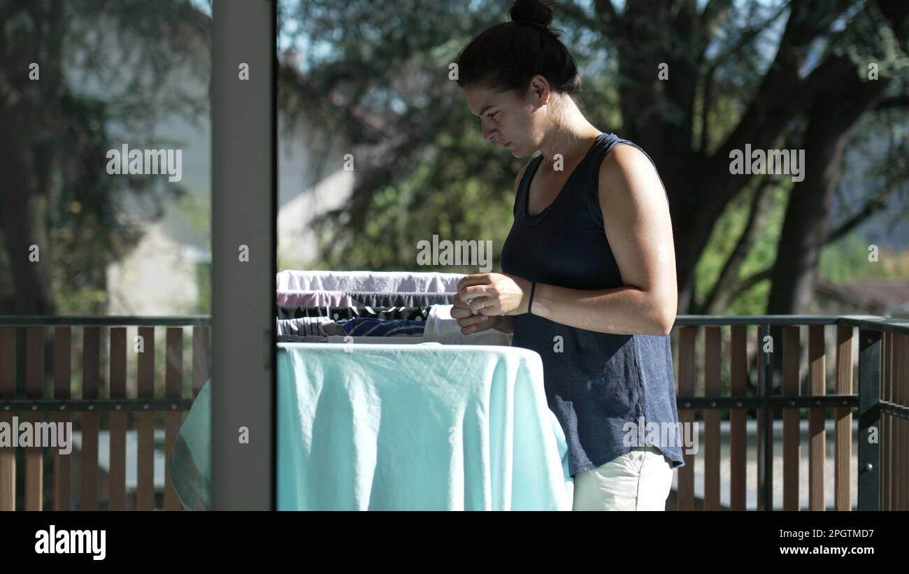 Woman putting wet clothes on clothesline to dry after laundry ...