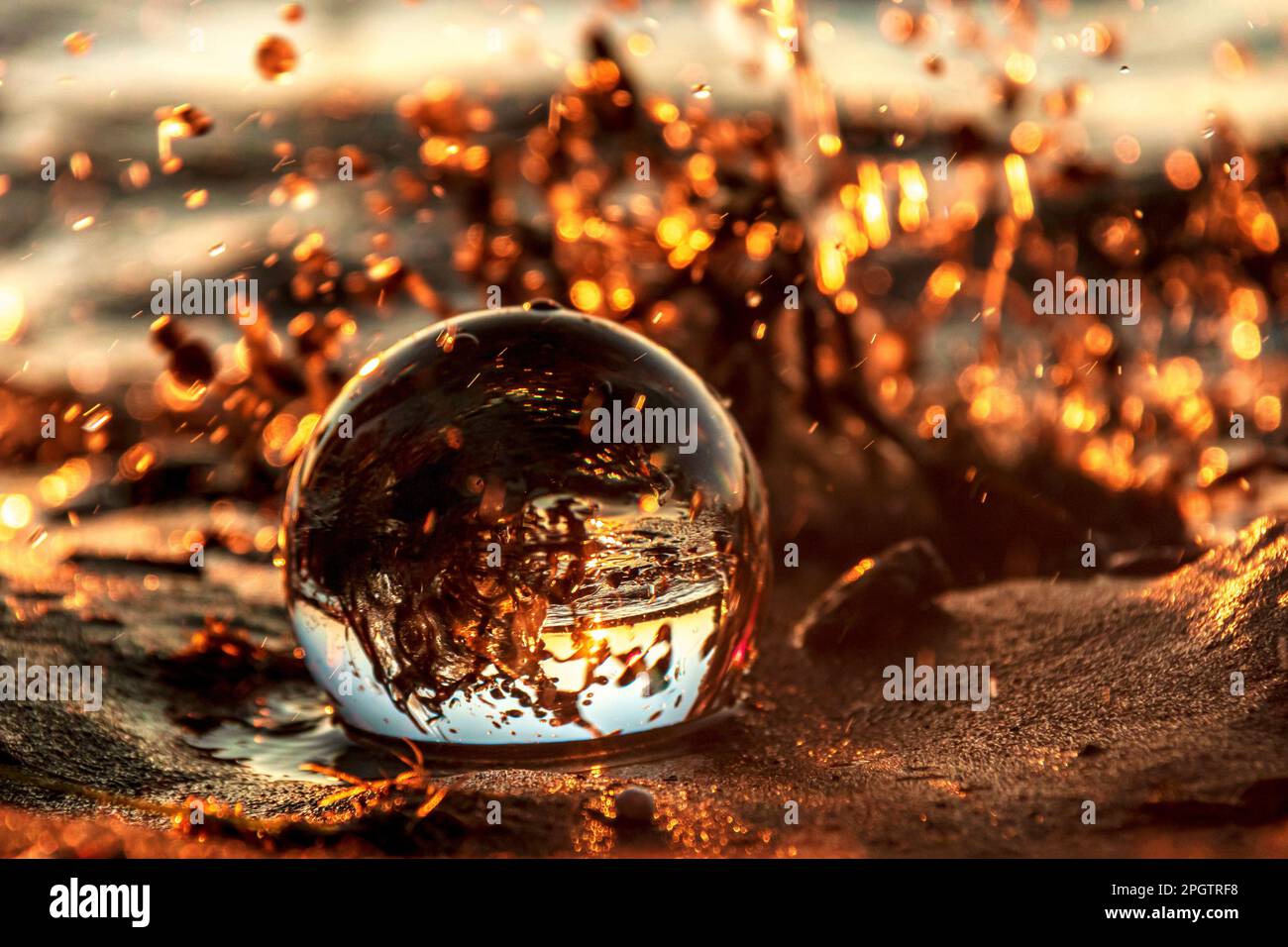 A bright orange and pink sunset illuminates a glass ball resting atop ...