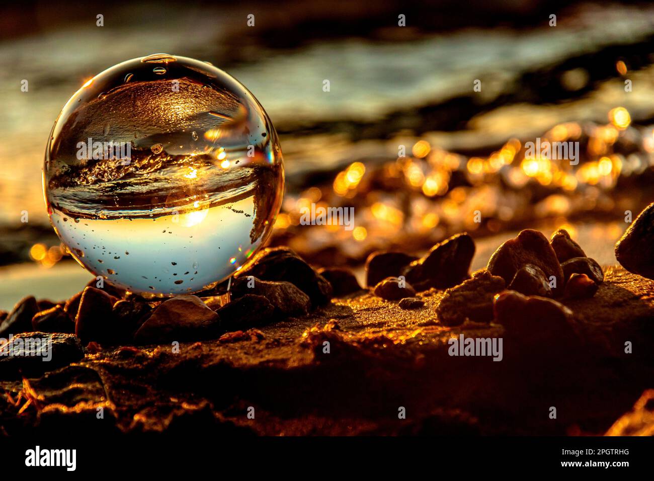 A bright orange and pink sunset illuminates a glass ball resting atop ...