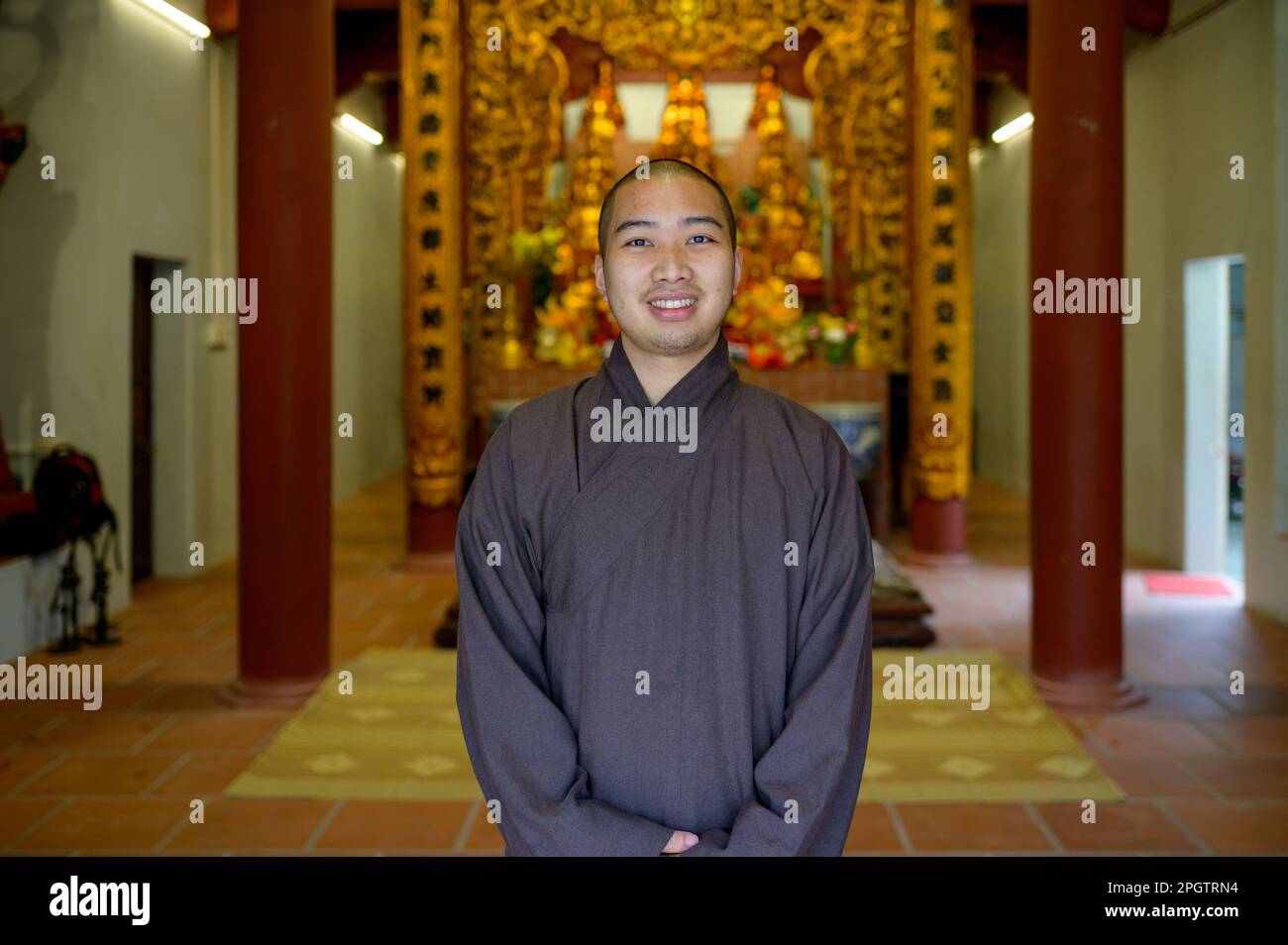 Smiling Asian monk in black robe looking at camera while standing ...