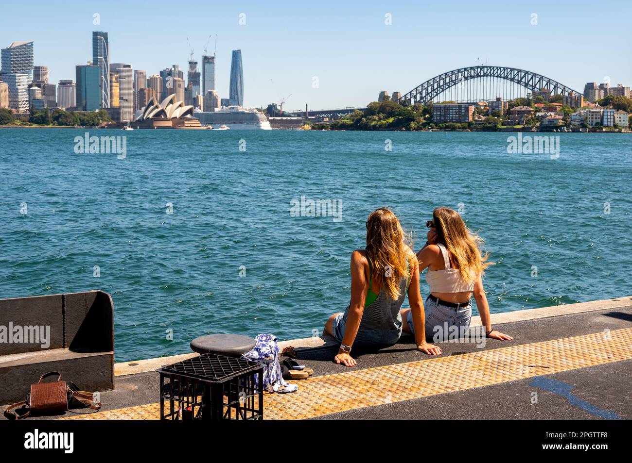Two young female holiday makers sit on Cremorne Point Wharf waiting for ...