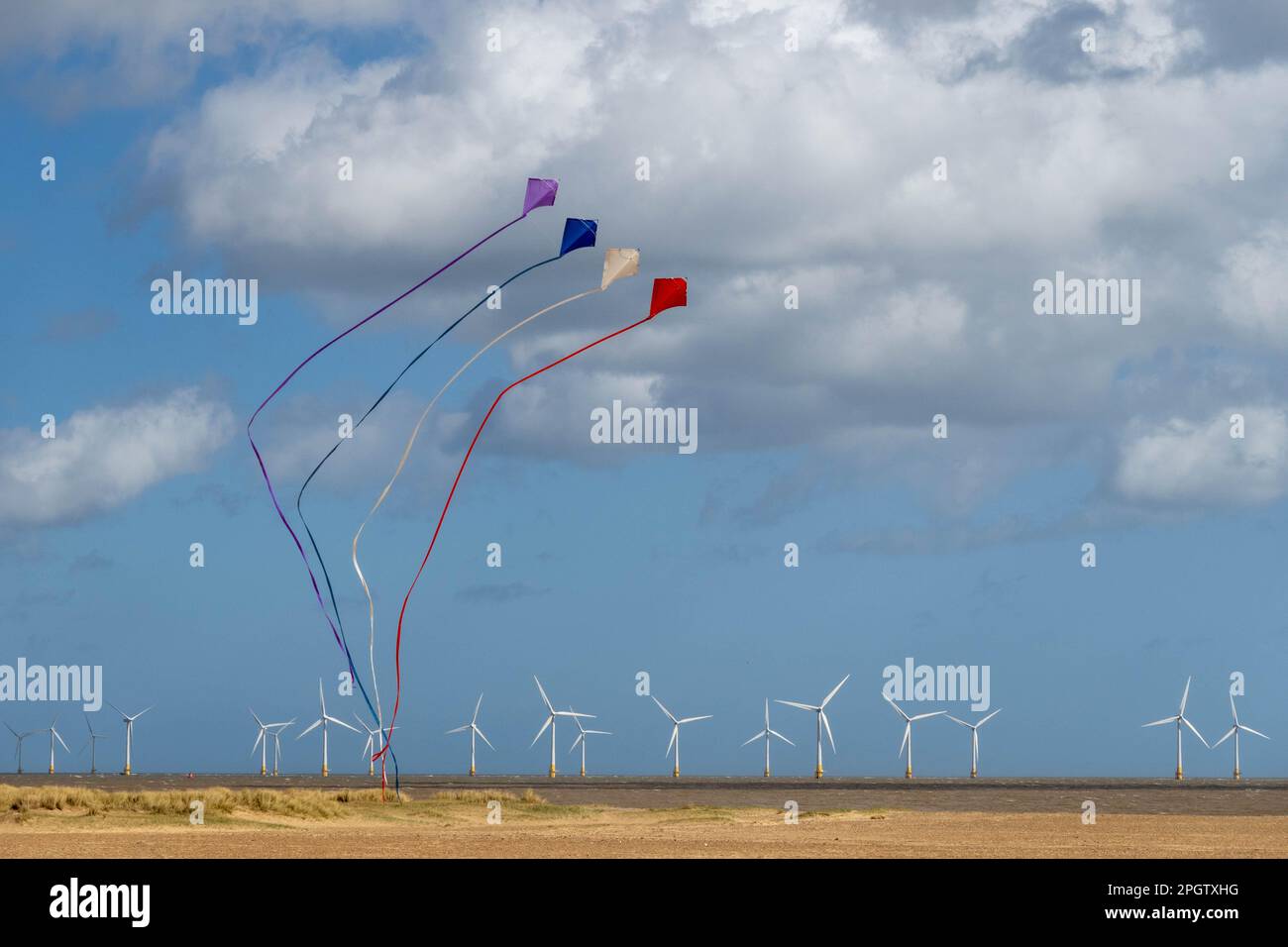 Quad line kite being flown on a beach in Norfolk with wind farm in ...
