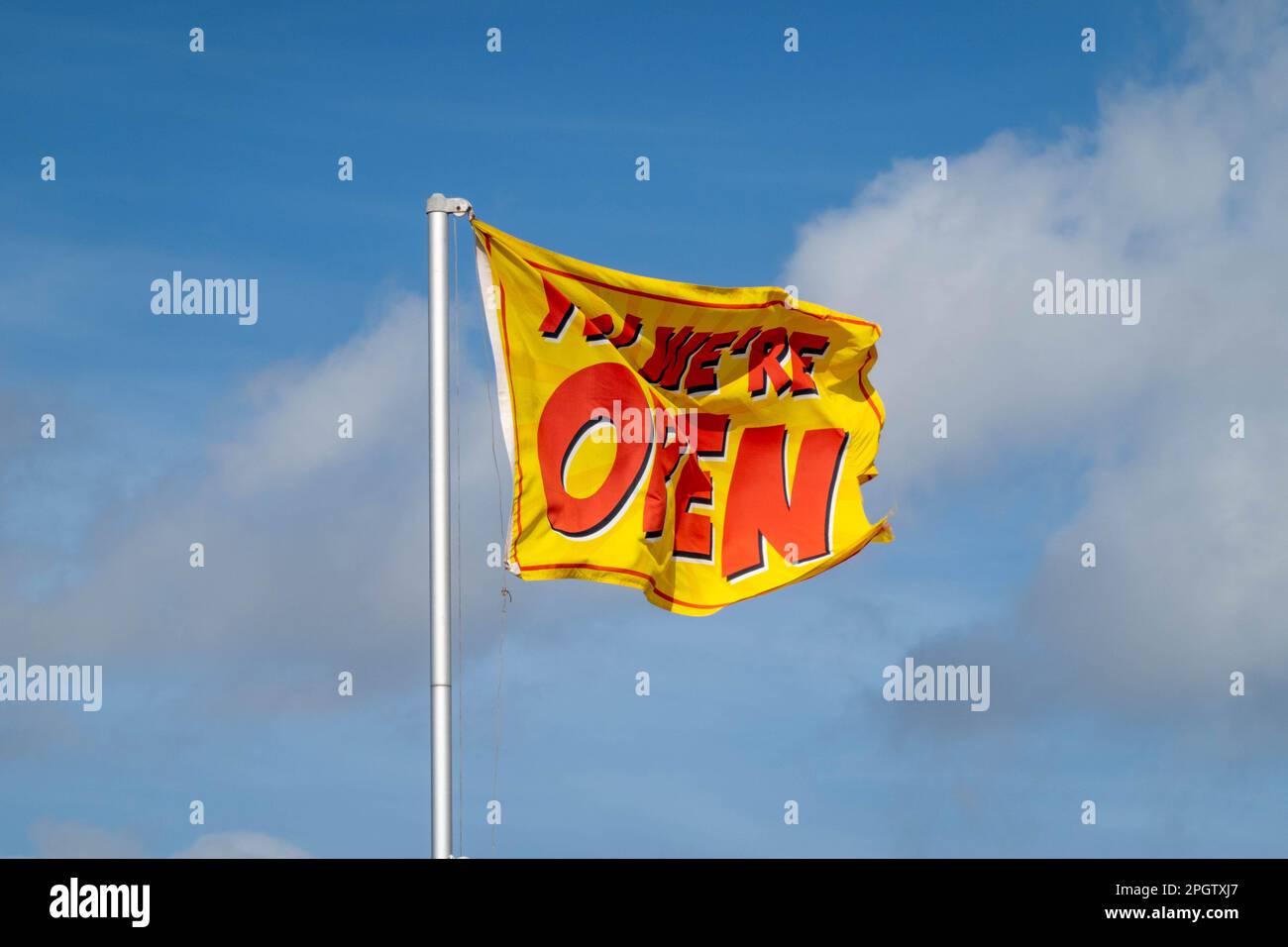 We Are Open flag blowing in the wind against a blue and white cloudy ...