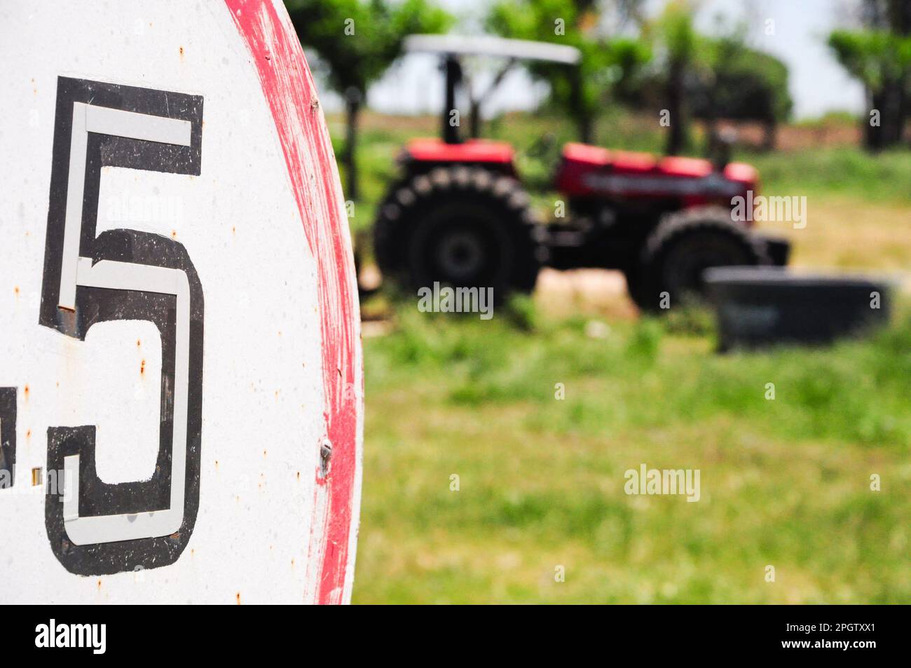 A 45k/h sign on the road, with a tractor on a farm in the background ...