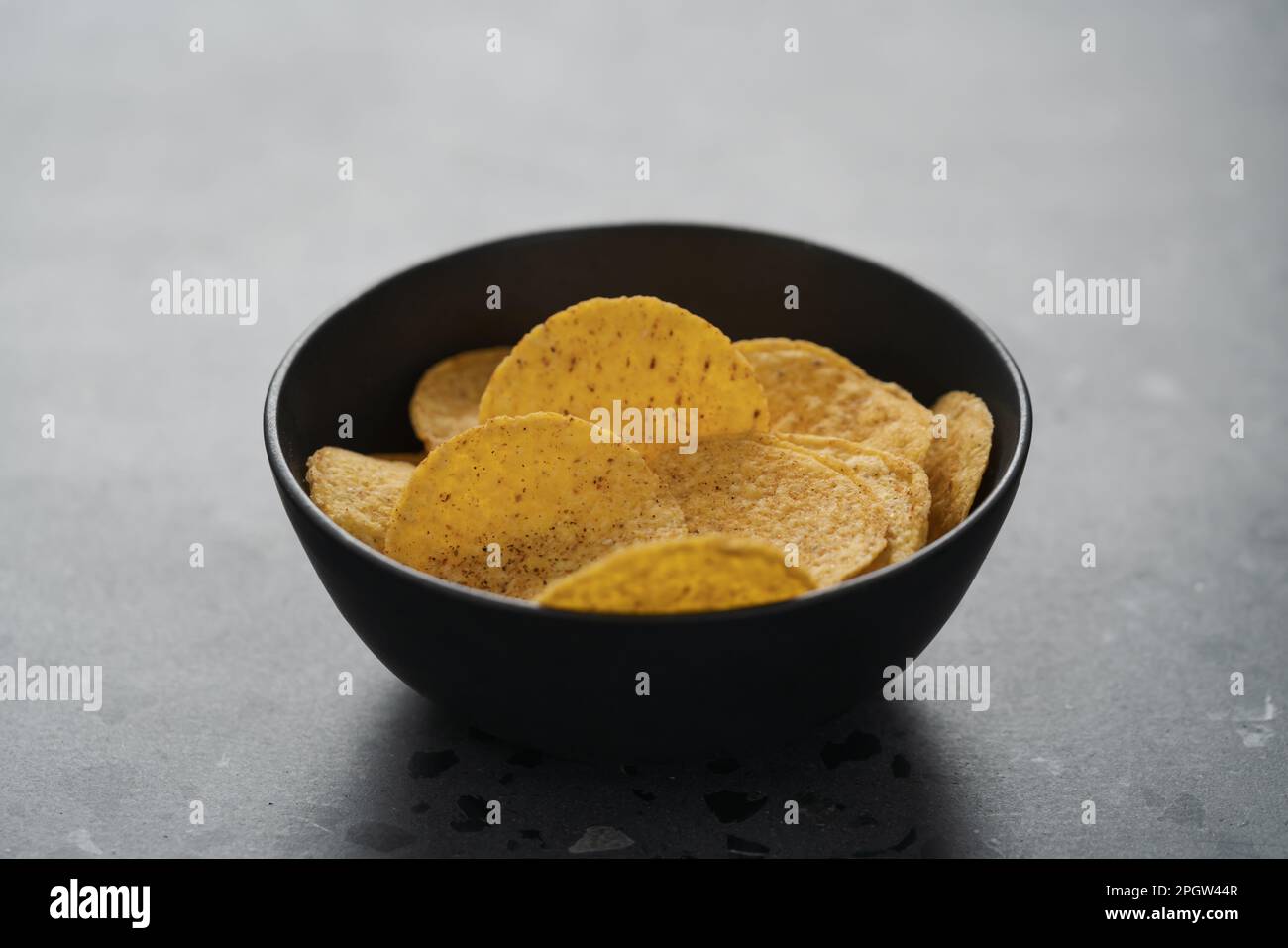 Round nachos in black ceramic bowl on concrete background, shallow ...